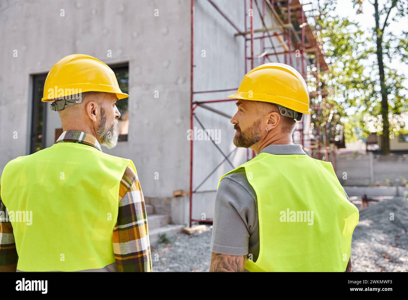 handsome cottage builders in safety helmets posing next to scaffolding ...