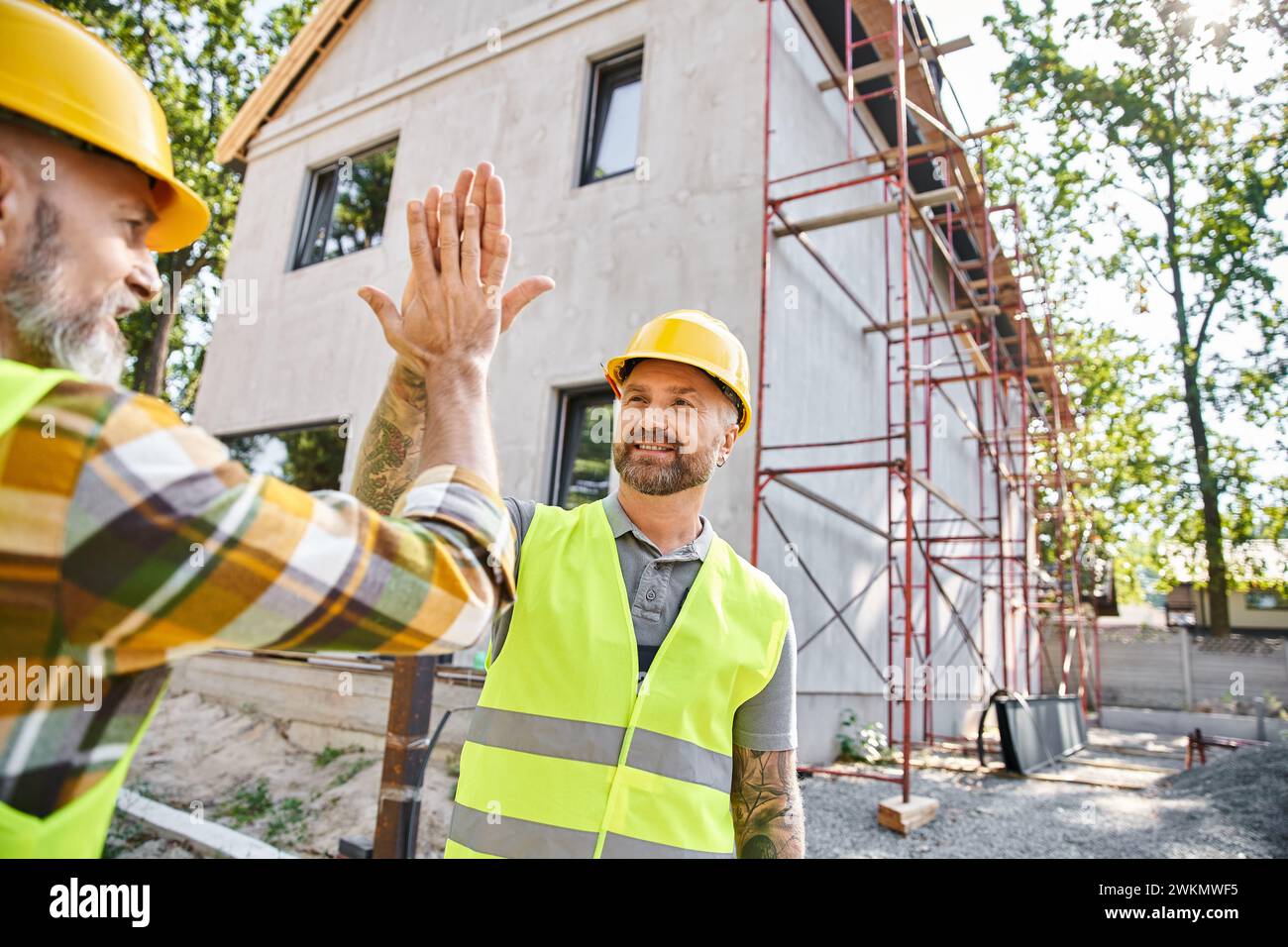 two cheerful cottage builders in safety attires giving high five to ...