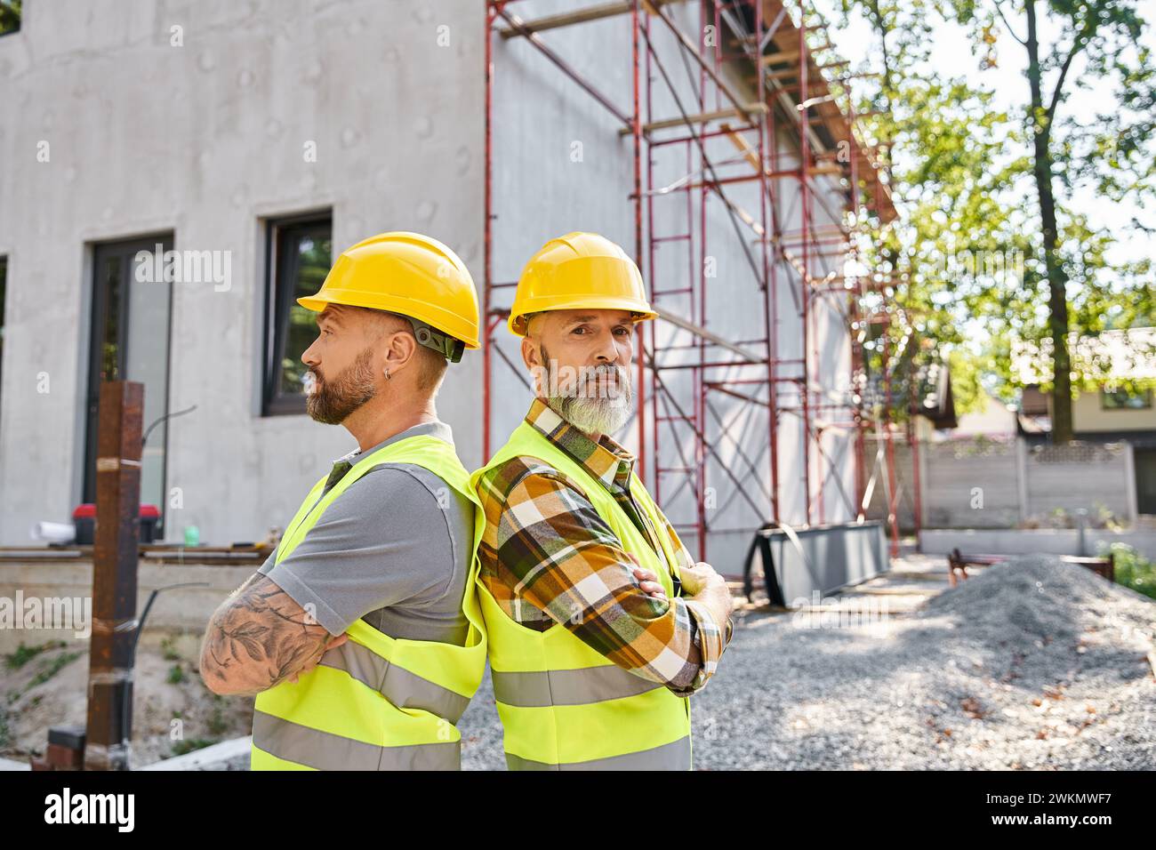 handsome cottage builders in safety vests posing back to back near ...