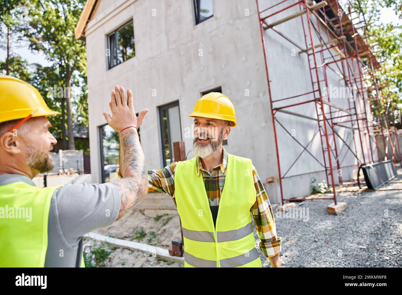 two cheerful cottage builders in safety attires giving high five to ...