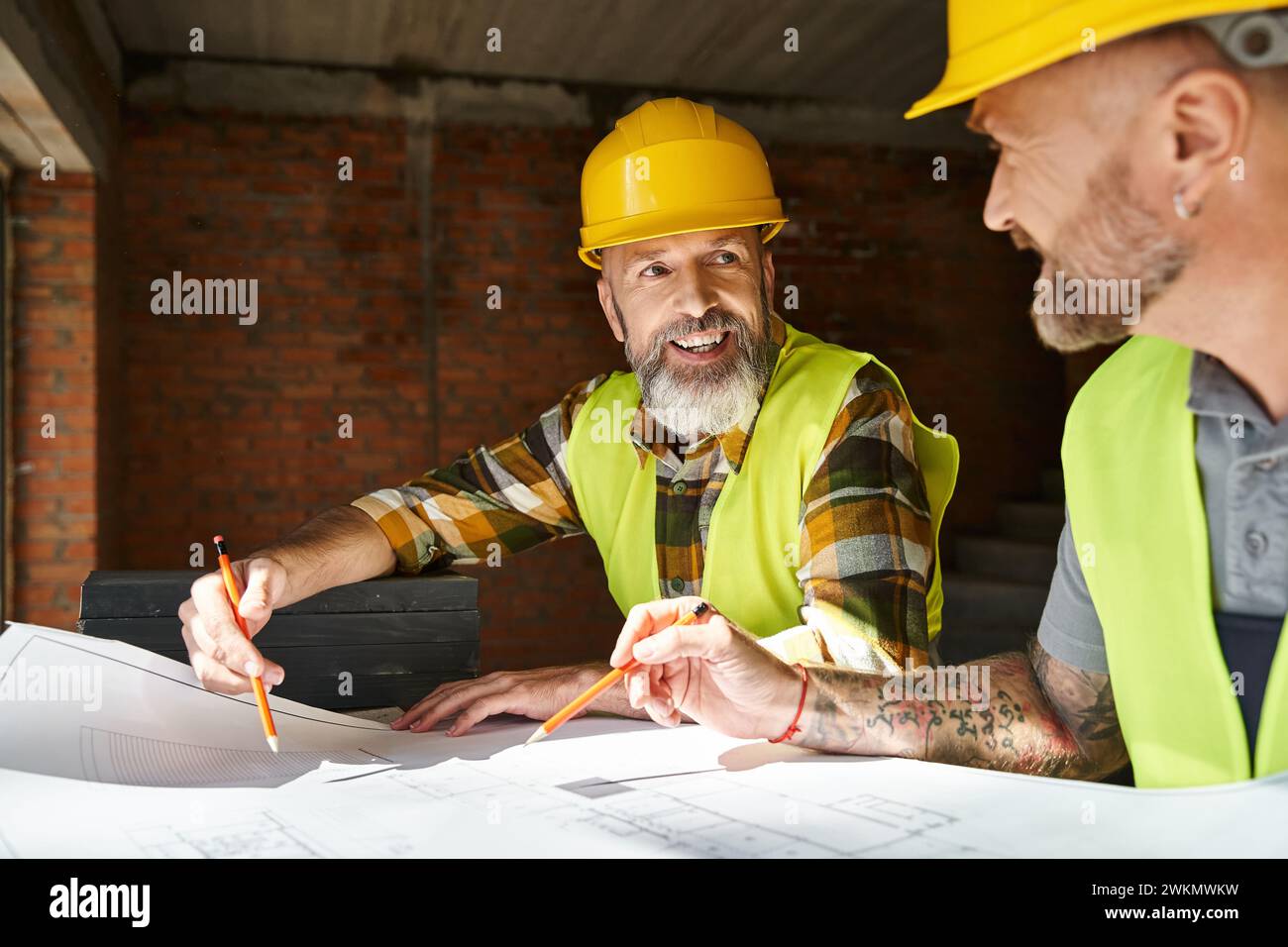 cheerful good looking builders in safety vests and helmets looking at ...