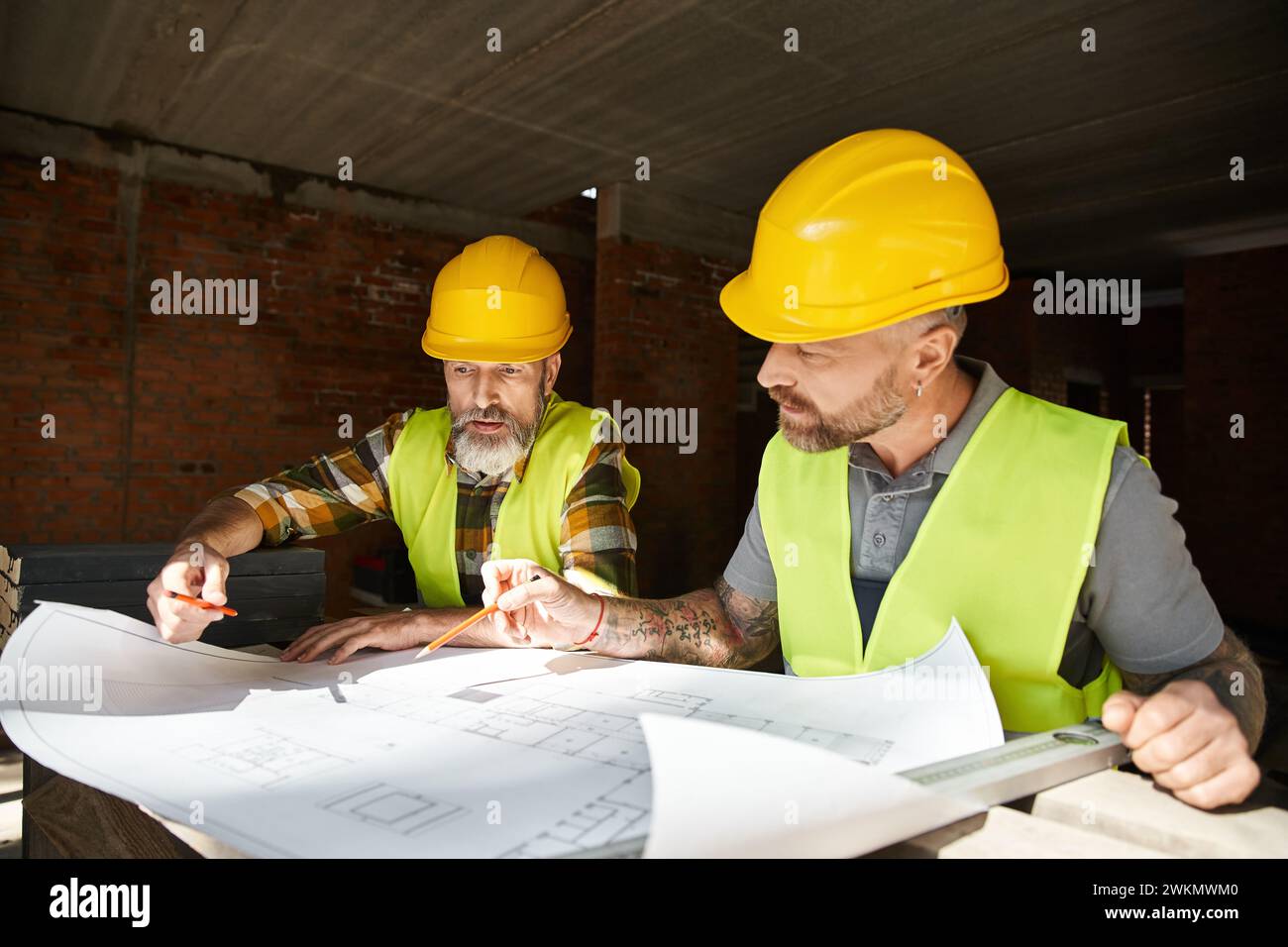 two handsome builders in safety helmets and vests working with ...