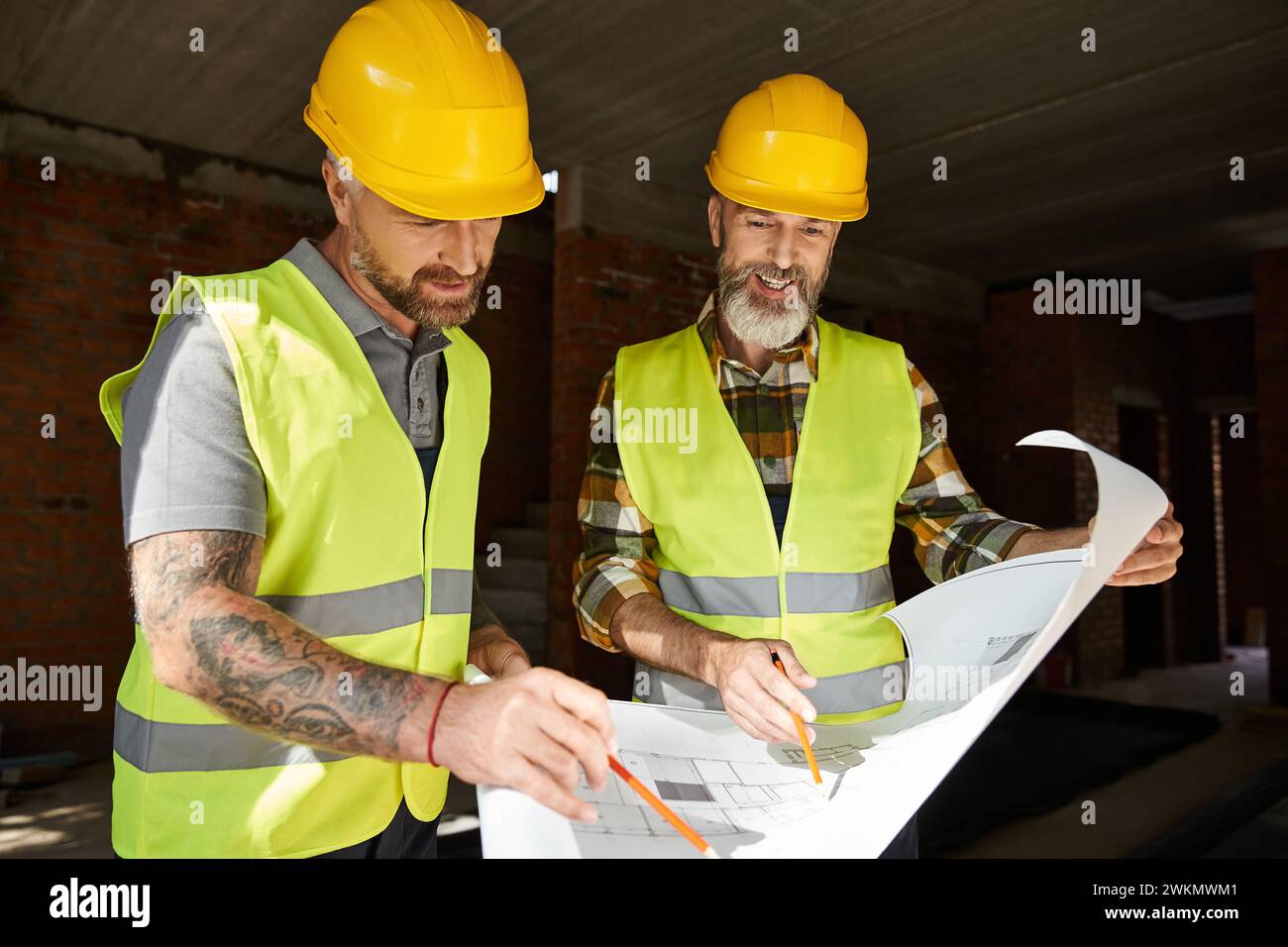 cheerful good looking builders in safety vests and helmets looking at ...