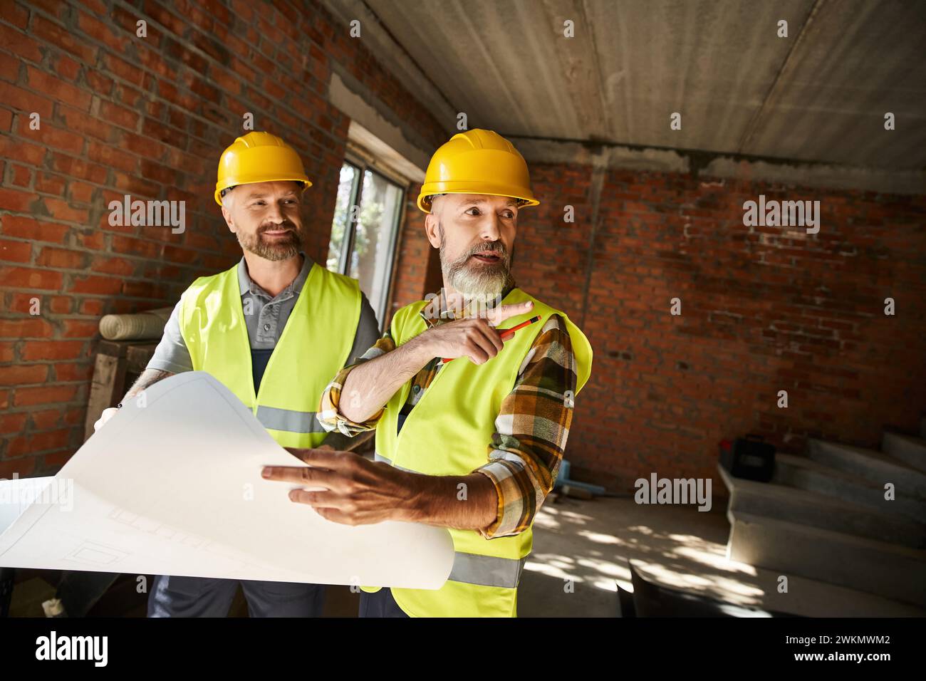 cheerful good looking builders in safety vests and helmets looking at ...