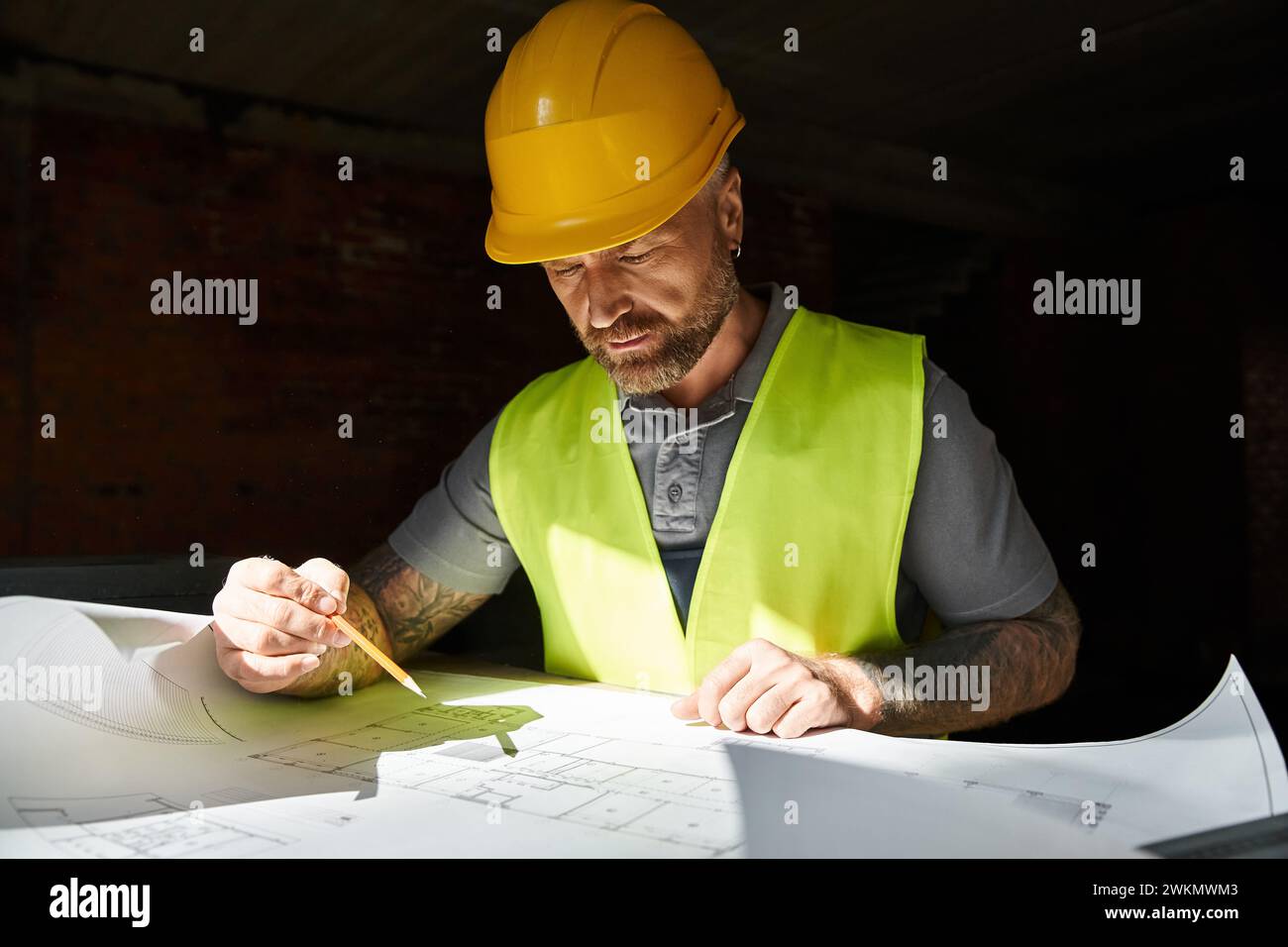 good looking builder in safety vest and helmet working on his blueprint ...