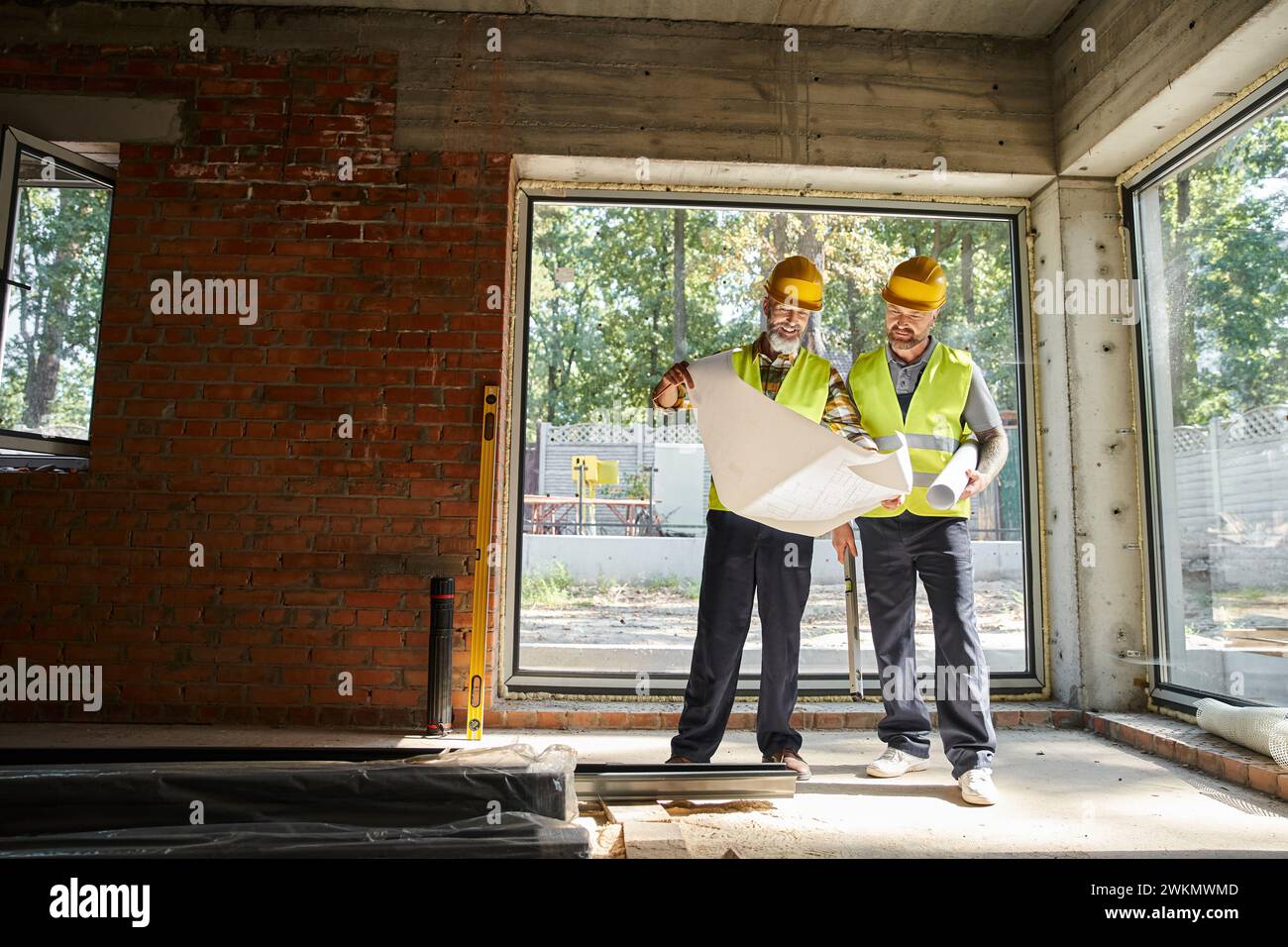 cheerful bearded men in safety helmets looking at blueprint while on ...