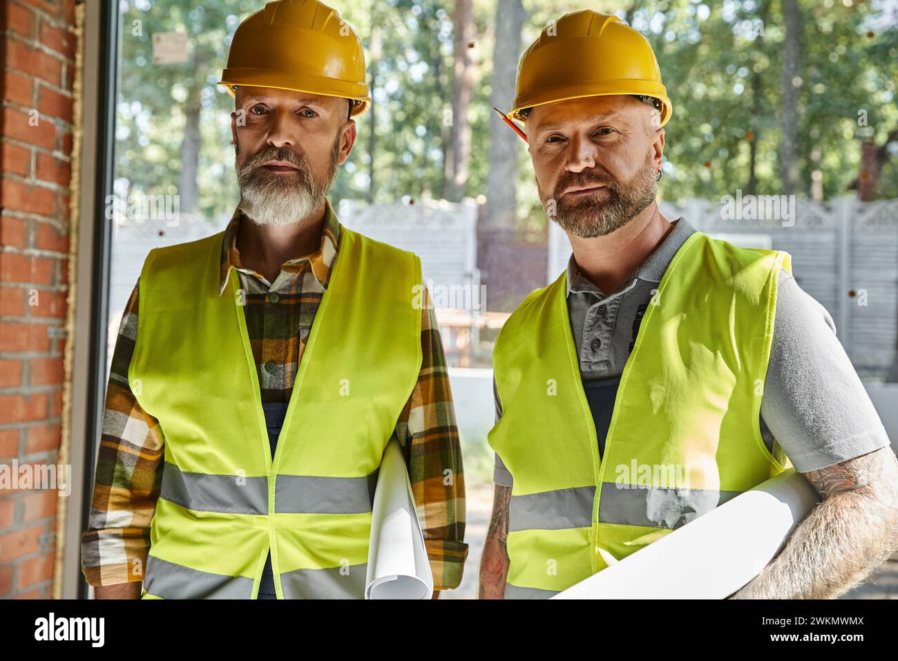 good looking dedicated builders in safety vests and helmets looking at camera on construction ...