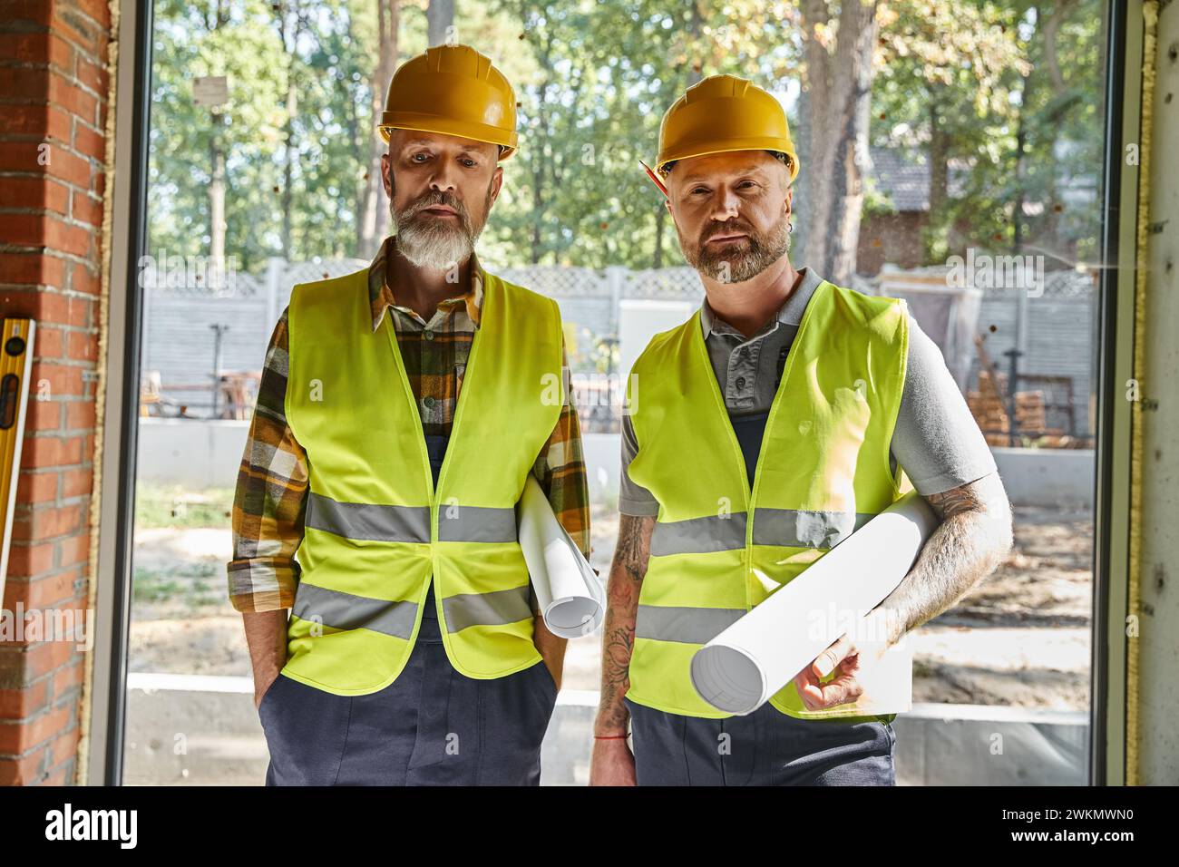 good looking dedicated builders in safety vests and helmets looking at camera on construction ...