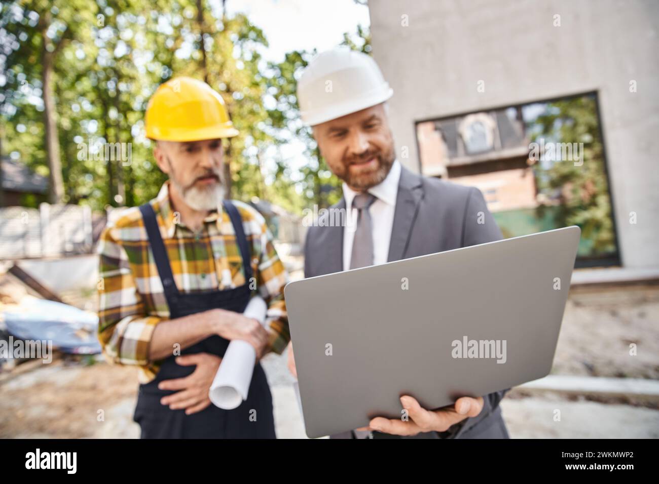 focus on laptop in hands of blurred architect and builder in safety ...
