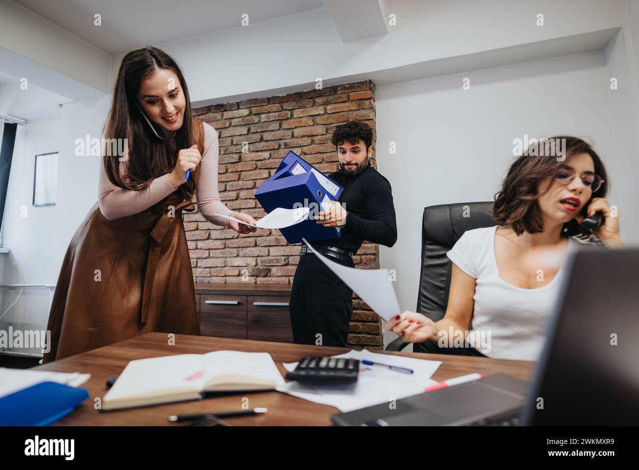 Busy office scene with a focused woman on the phone, a man sneaking up ...