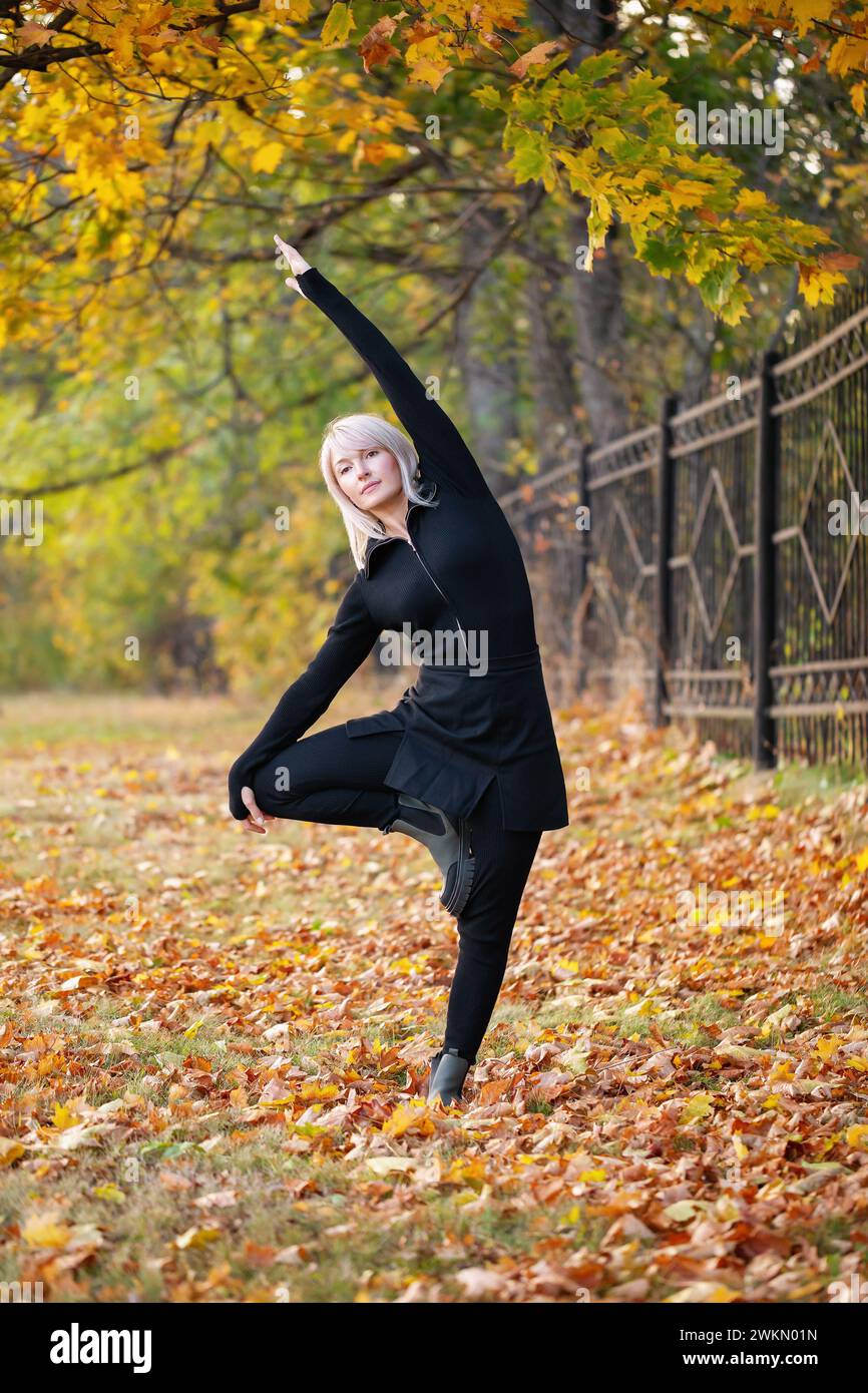 Attractive blonde woman performing a variation of vrikshasana exercise ...
