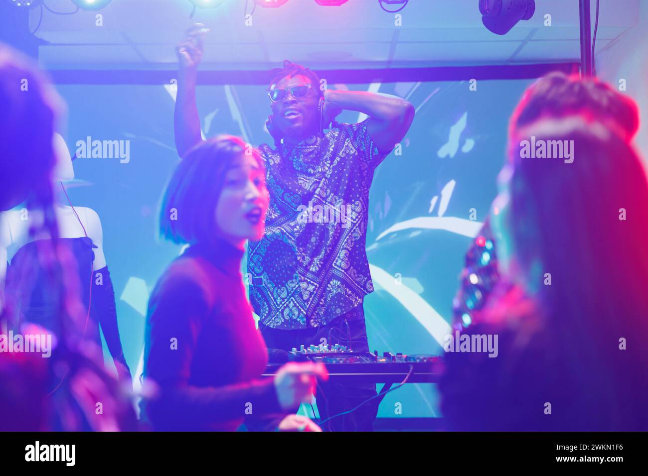 People partying on dancefloor while young dj performing on stage in ...