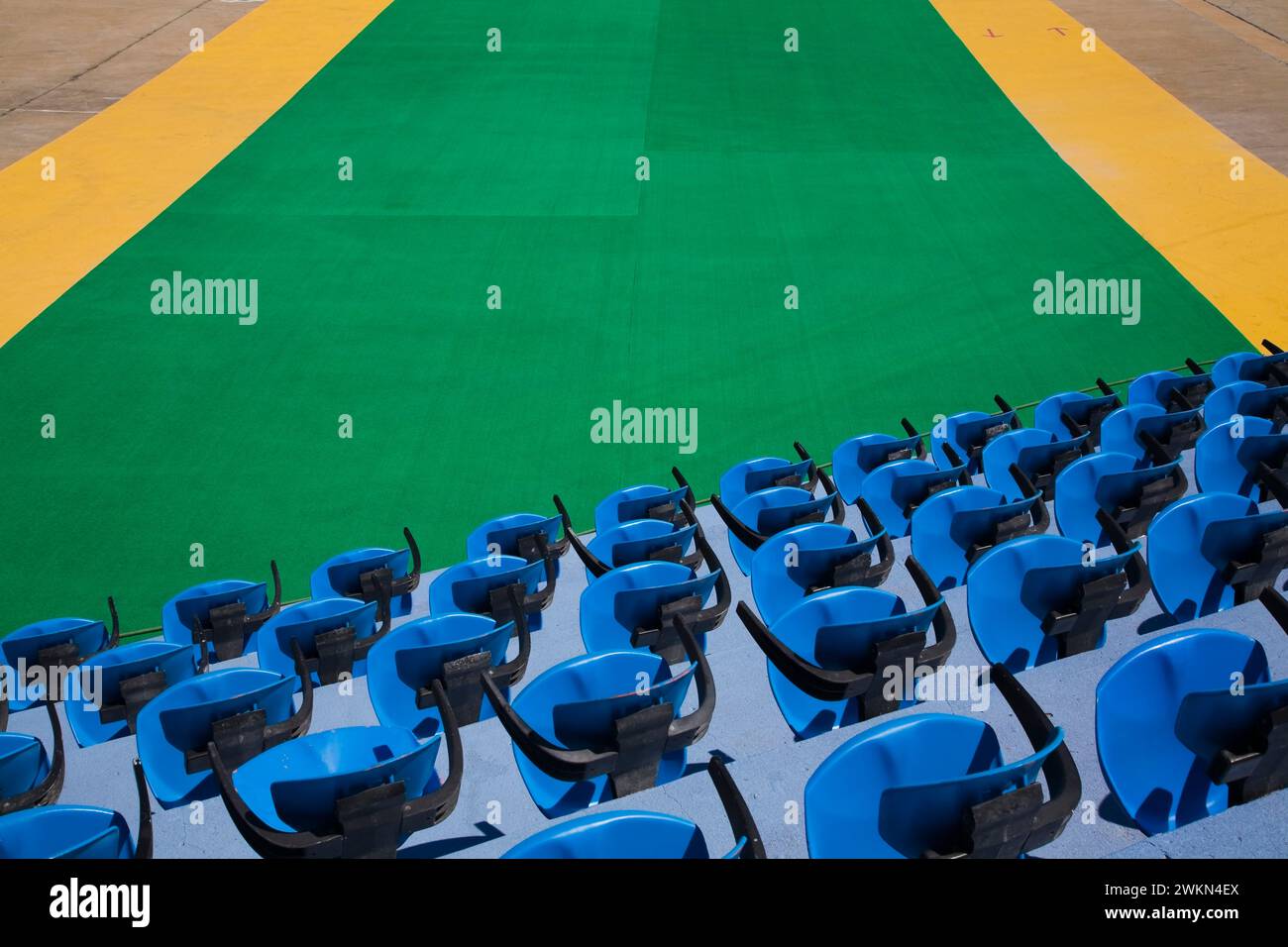 Empty blue folding spectator seats in front of synthetic green grass ...