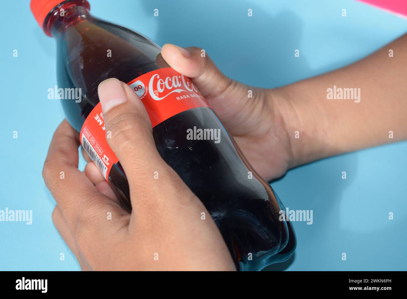 Close up view of a hand holding a Coca Cola product. Against a blue ...