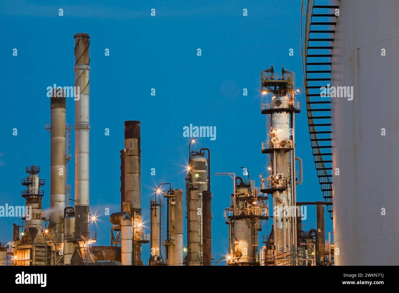 Smokestacks and storage tank at an oil and gas refinery at dusk ...