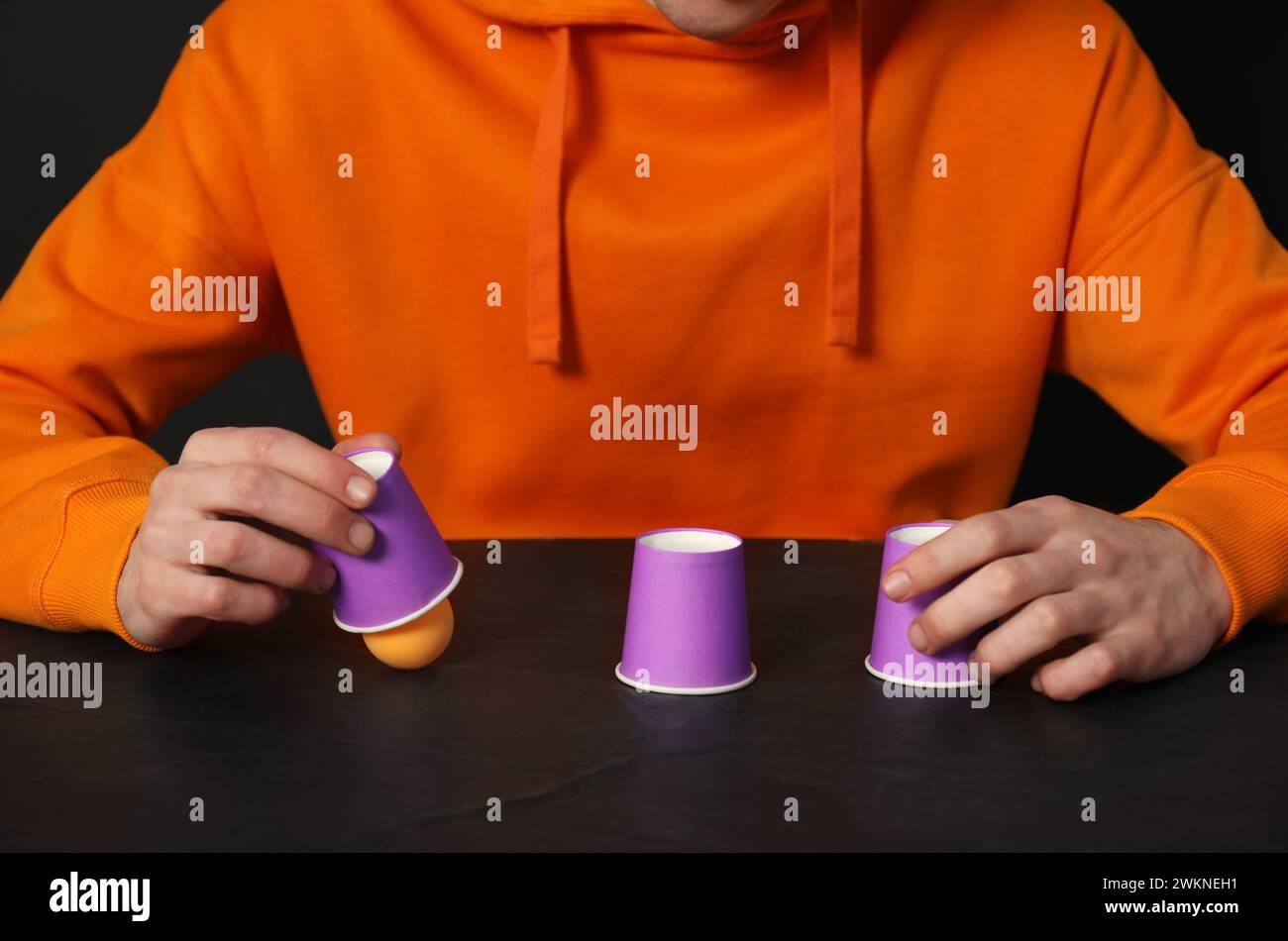 Shell game. Man showing ball under cup at black table, closeup Stock ...