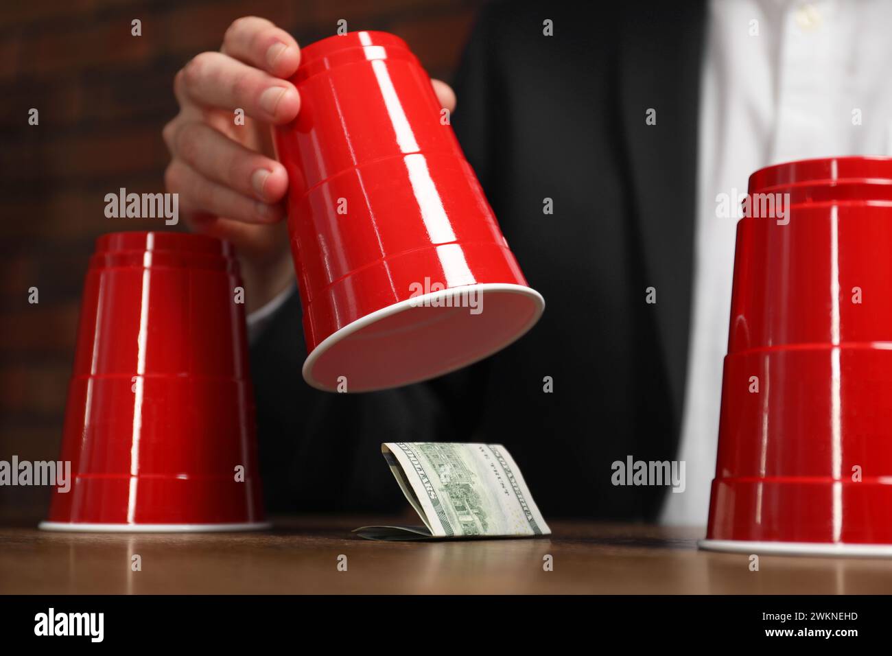 Shell game. Man showing dollar banknote under cup at wooden table ...