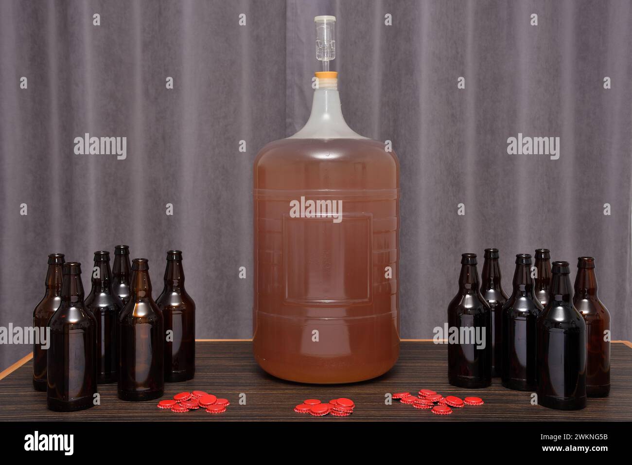 Home brewing carboy, beer bottles and red beer caps ready for ...