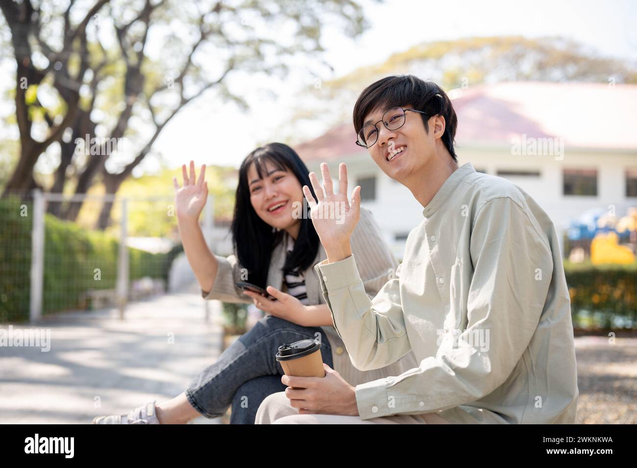 Two friendly and cheerful Asian friends or colleagues are waving their ...