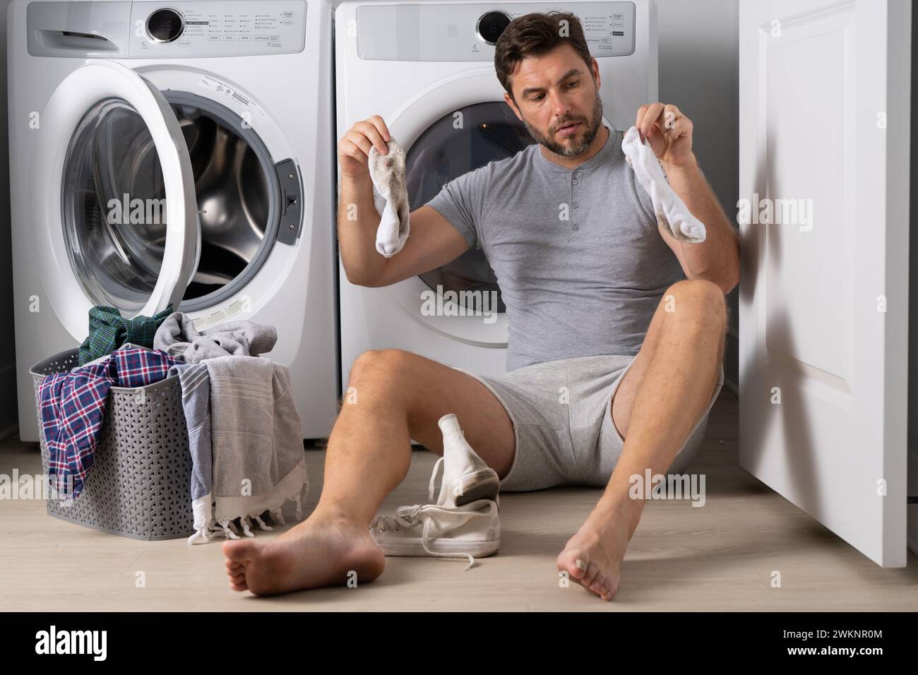 Man with clothes near washing machine. Handsome man sits in front of ...