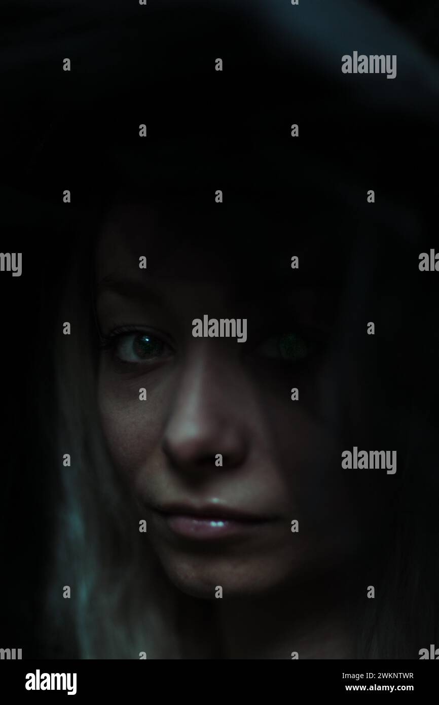 A dark, intimate portrait of a woman partially obscured by her hat ...