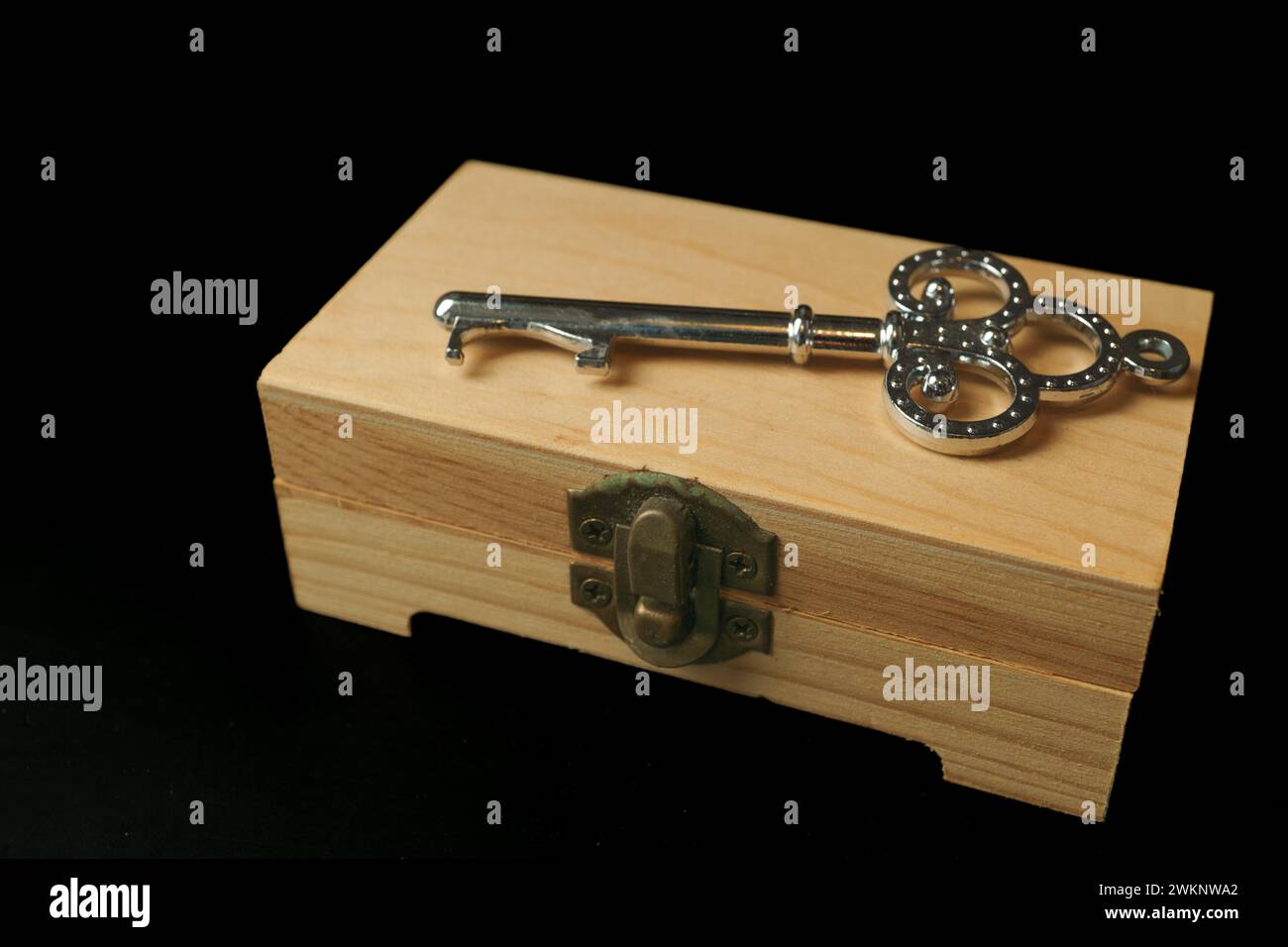 Closed wooden box with a metal key on top isolated on black background ...