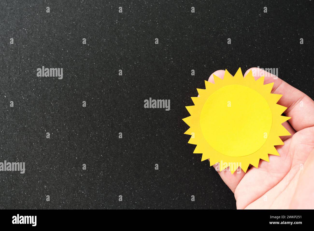 Human hand holding bright yellow sun cutout in black background. Light ...