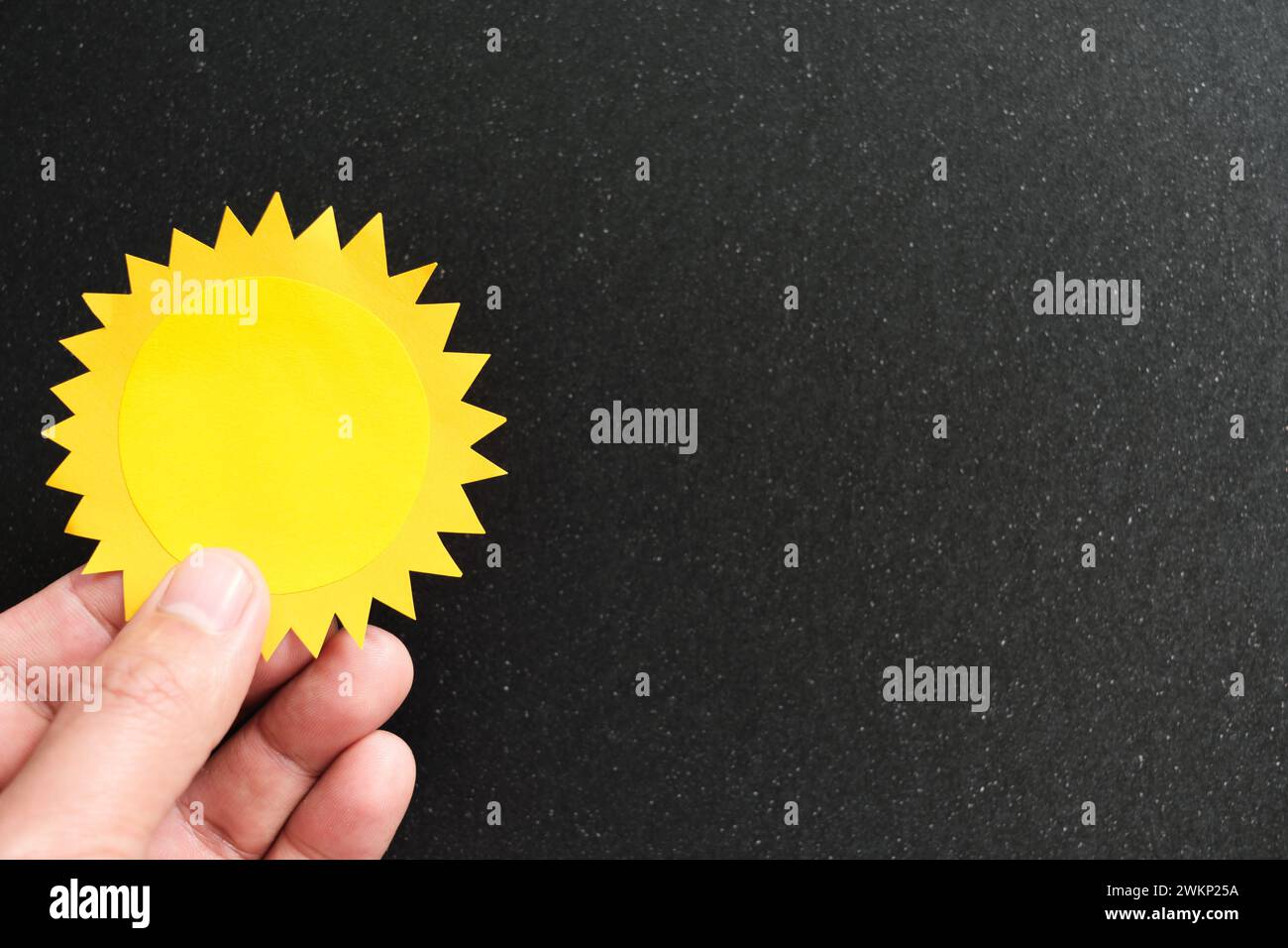 Human hand holding bright yellow sun cutout in black background. Light ...
