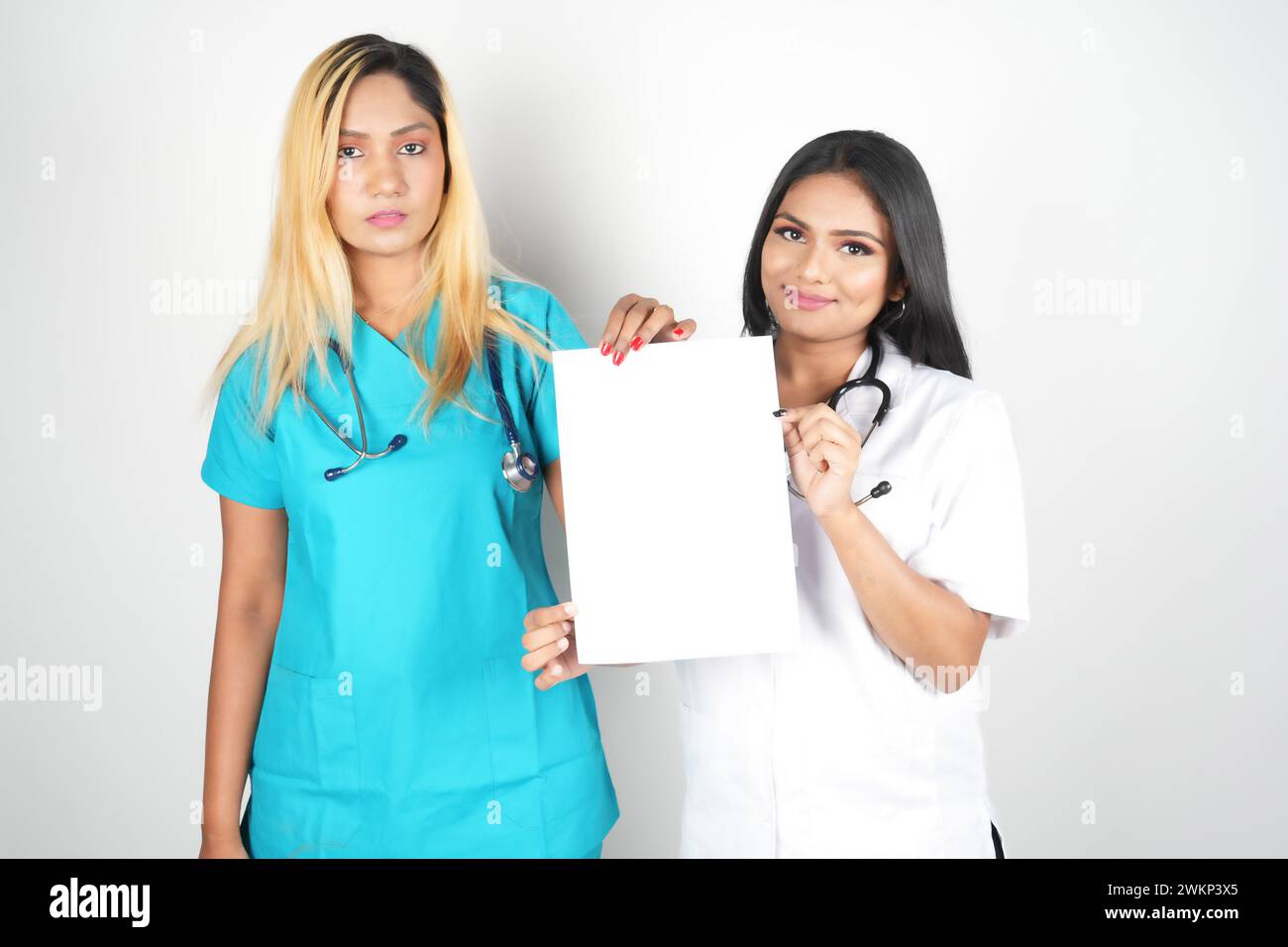 Two female healthcare professionals in scrubs posing with a blank sign ...