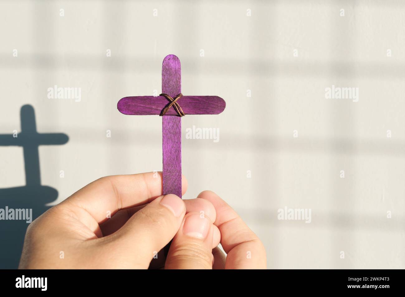 Male hand holding purple wooden cross with shadow. Christianity, faith ...