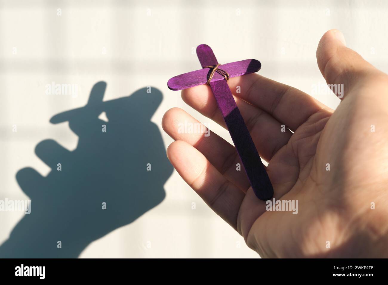 Male hand holding purple wooden cross with shadow. Christianity, faith ...