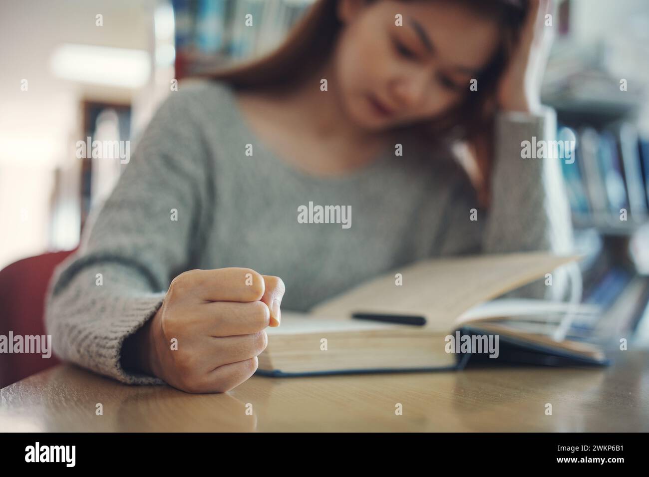 Stressed woman student with clenched fist reading a book at table ...