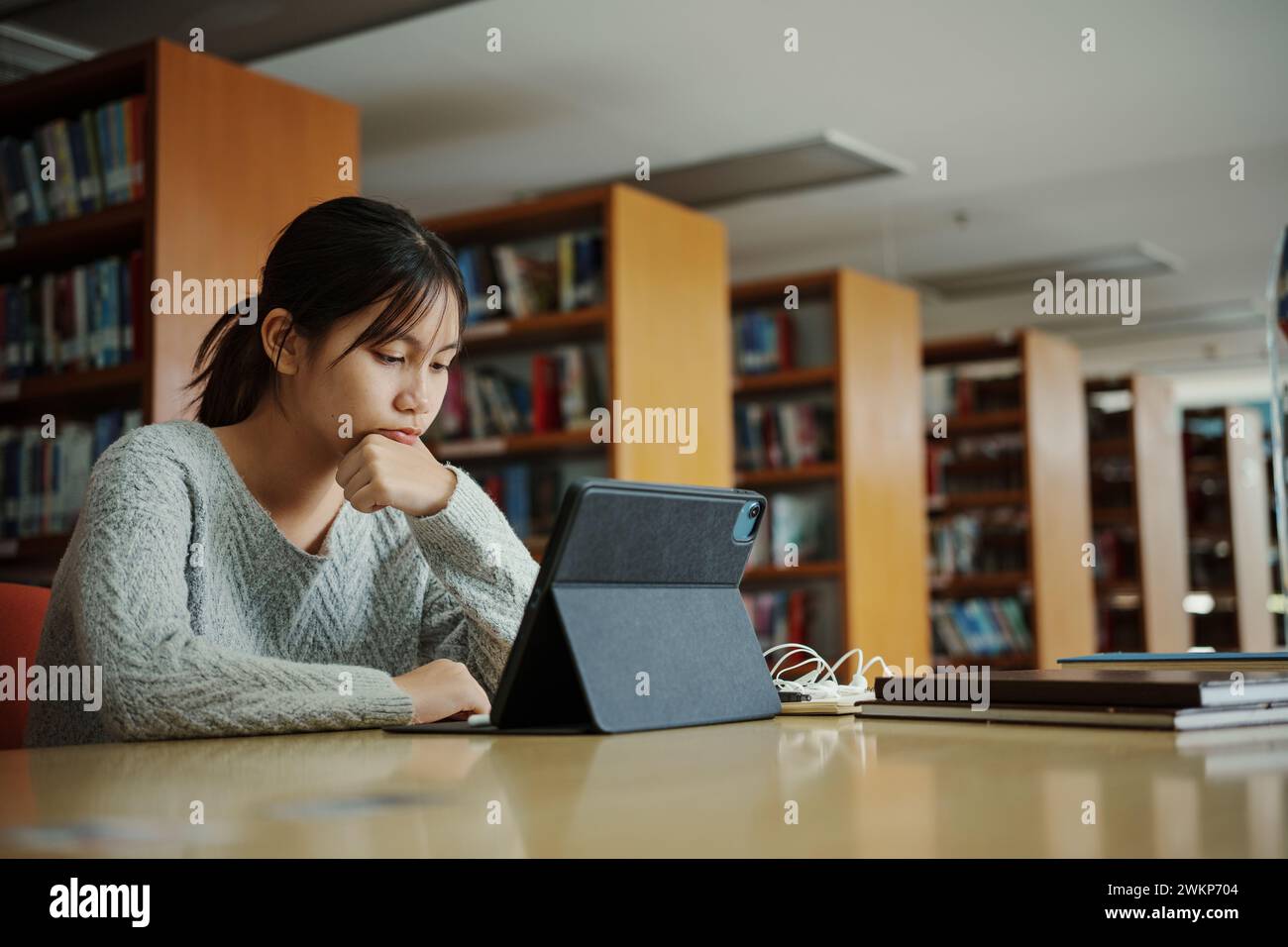 Stressed young female student sitting at wooden table and reading book ...