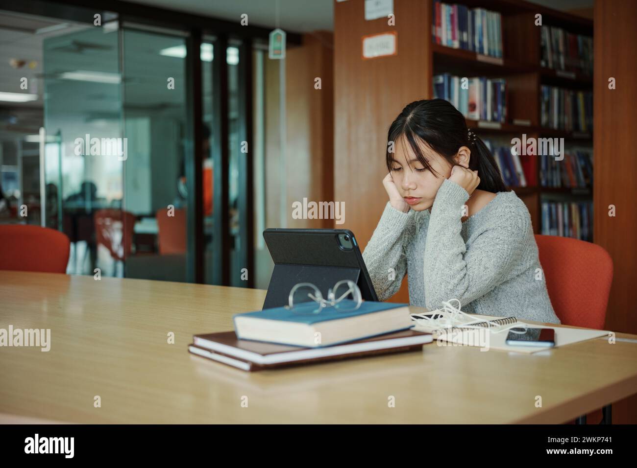 Stressed young female student sitting at wooden table and reading book ...