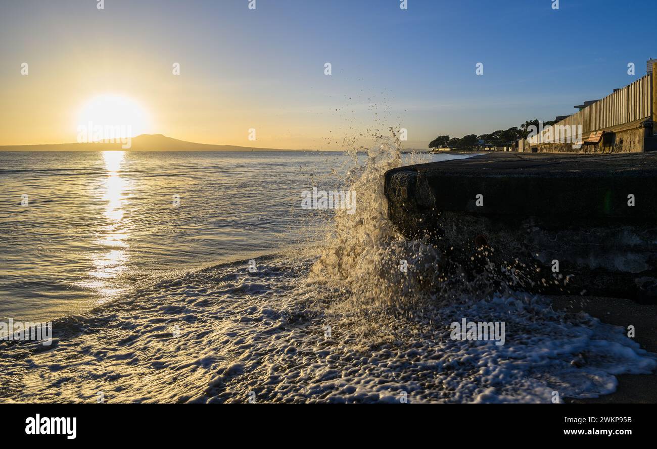 Waves crashing into the concrete seawall. Sunrise over Rangitoto Island ...