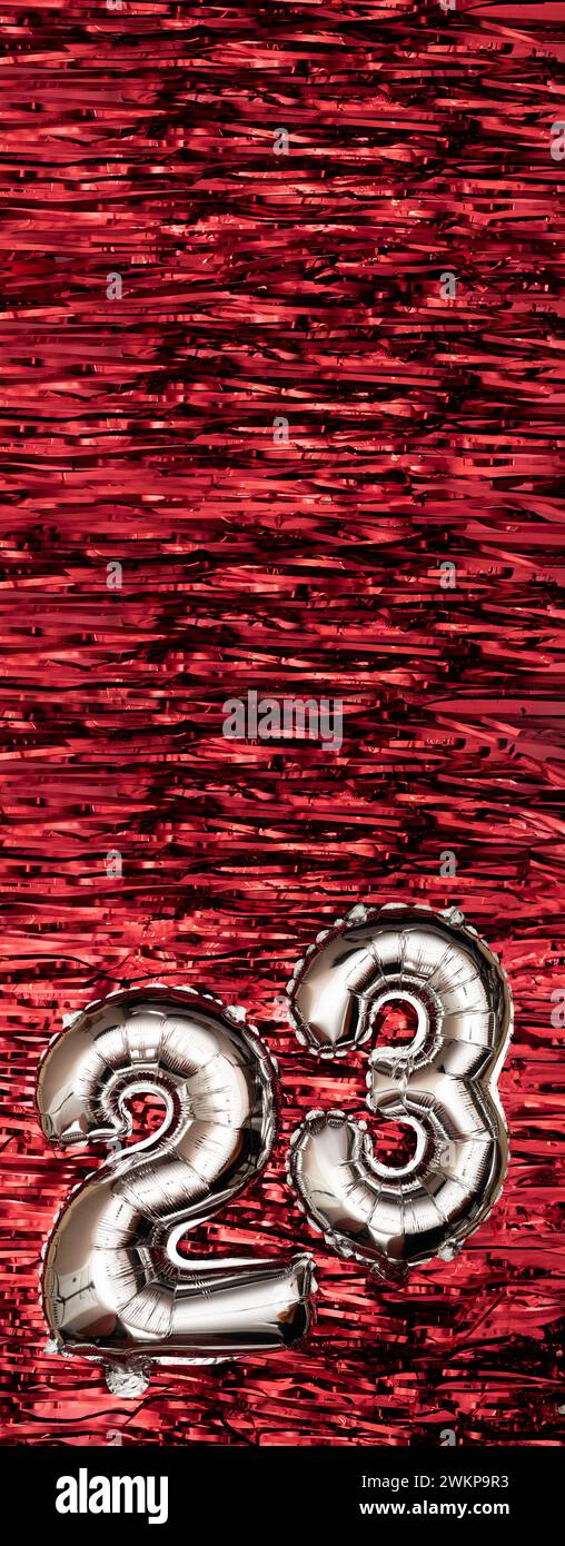 Silver foil balloon number number 23 on a background of red tinsel ...