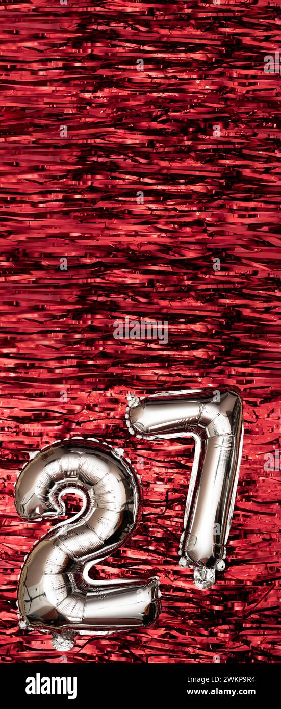 Silver foil balloon number number 27 on a background of red tinsel ...