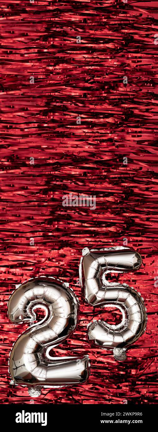 Silver foil balloon number number 25 on a background of red tinsel ...