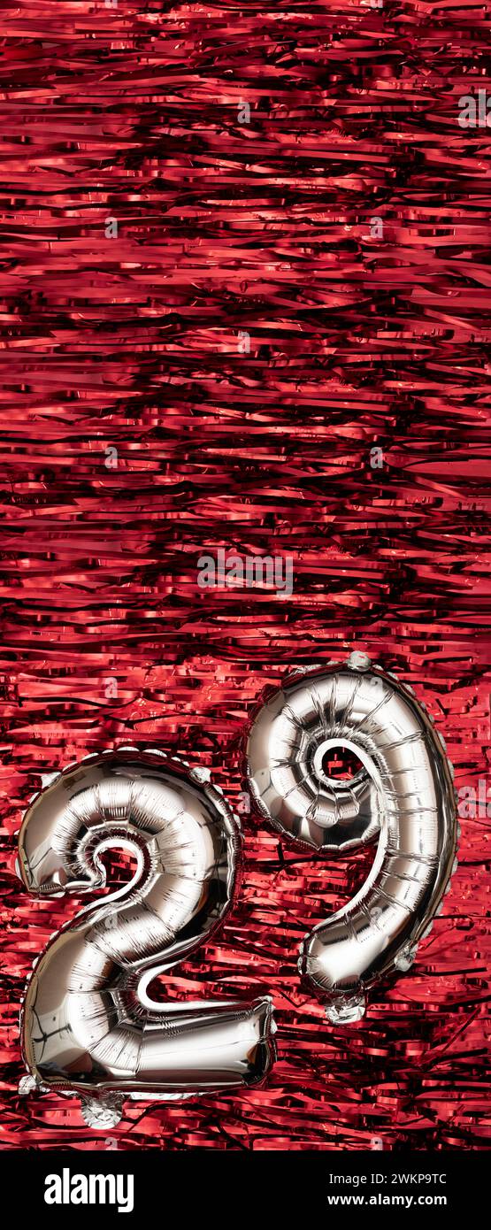 Silver foil balloon number number 29 on a background of red tinsel ...