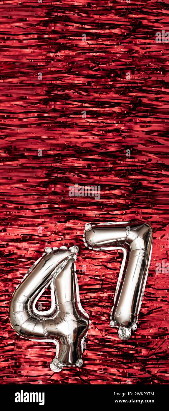 Silver foil balloon number number 47 on a background of red tinsel ...