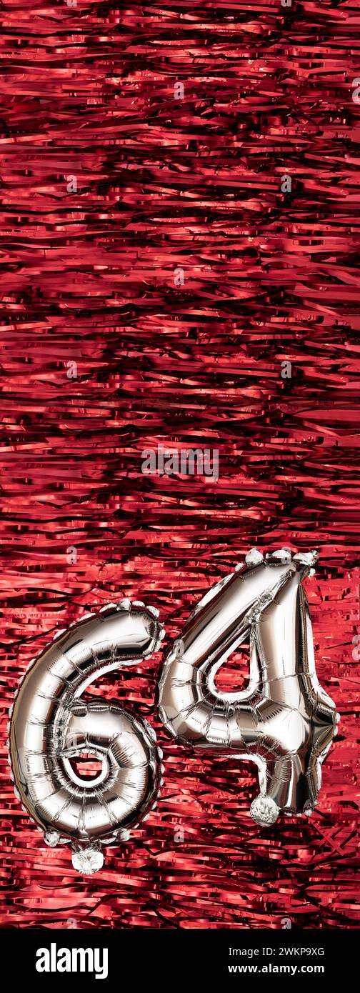 Silver foil balloon number 64 on a background of red tinsel decoration ...
