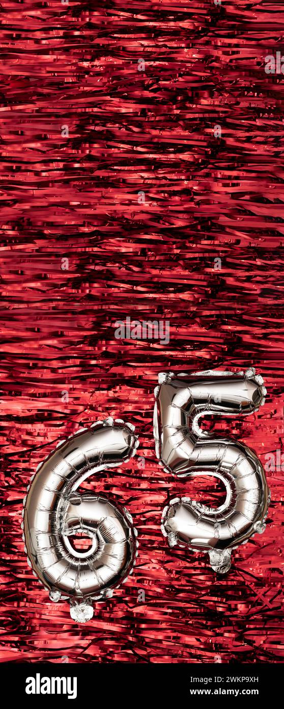 Silver foil balloon number 65 on a background of red tinsel decoration ...