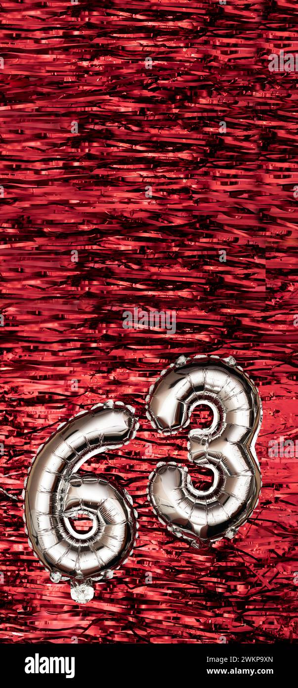 Silver foil balloon number 63 on a background of red tinsel decoration ...