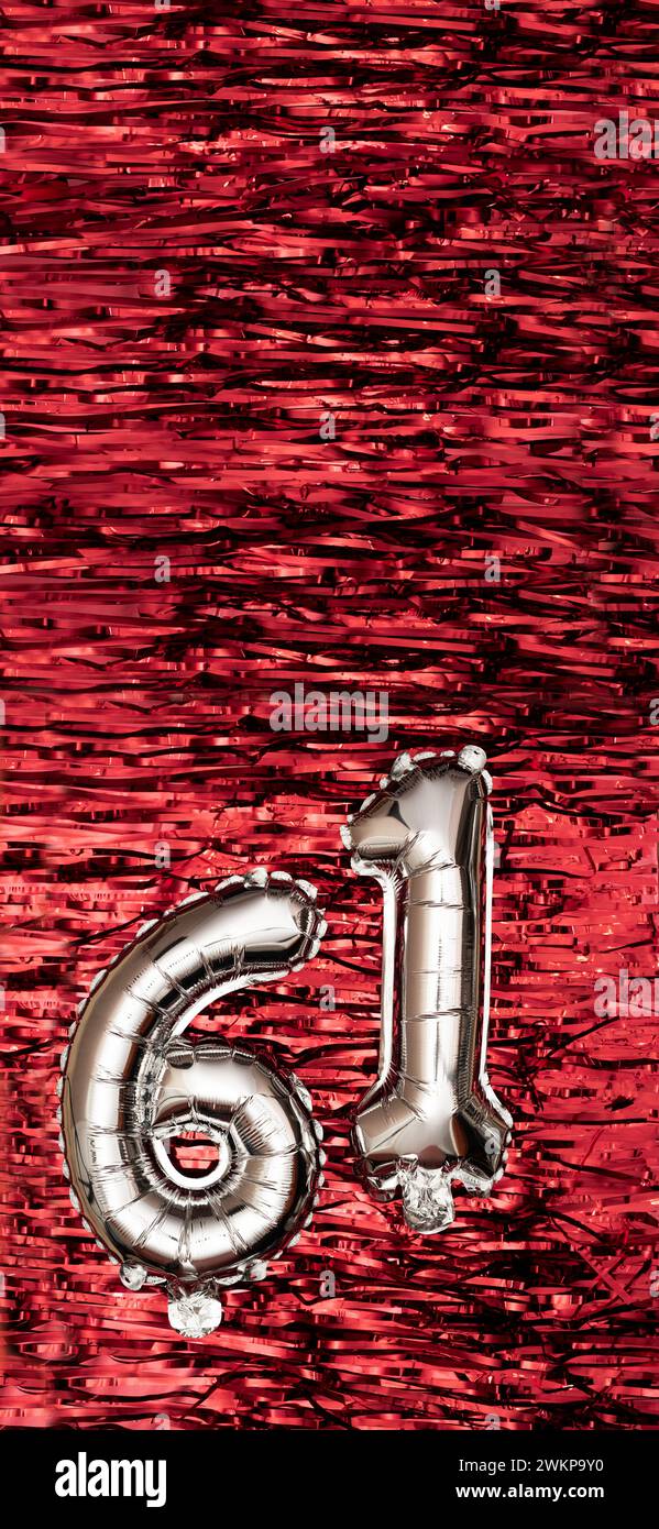 Silver foil balloon number 61 on a background of red tinsel decoration ...
