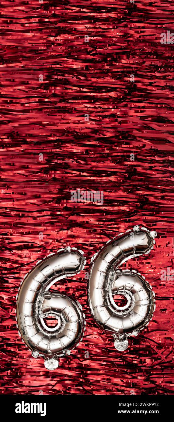 Silver foil balloon number 66 on a background of red tinsel decoration ...