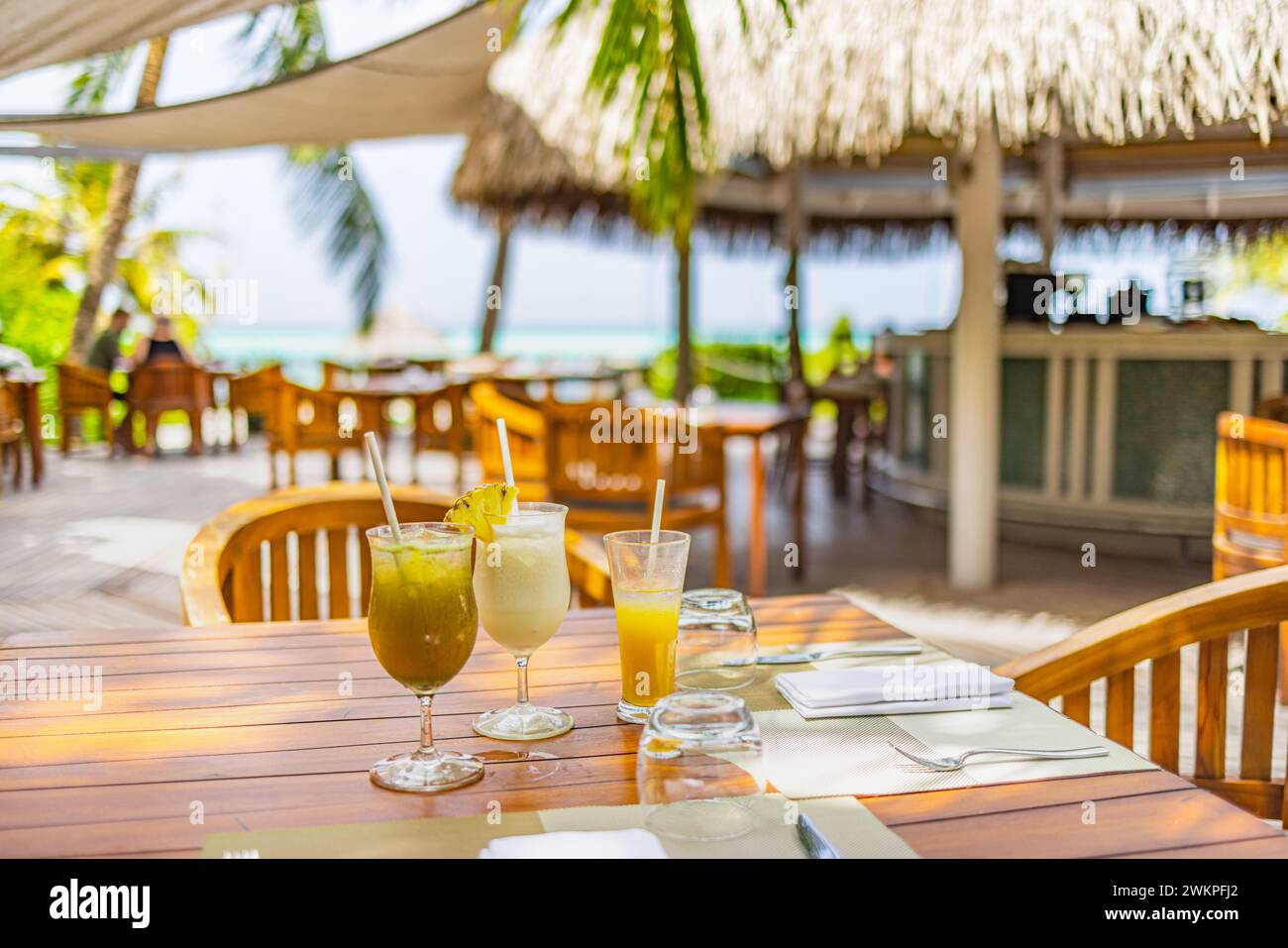 Outdoors tropical restaurant with wooden tables, chairs under palm ...