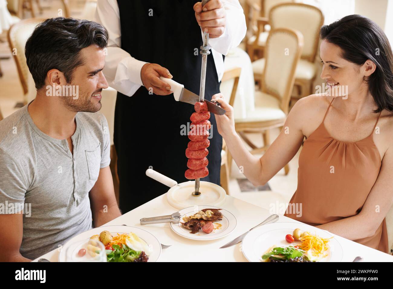 Couple, restaurant and waiter serving food or sausage kebab on skewer ...