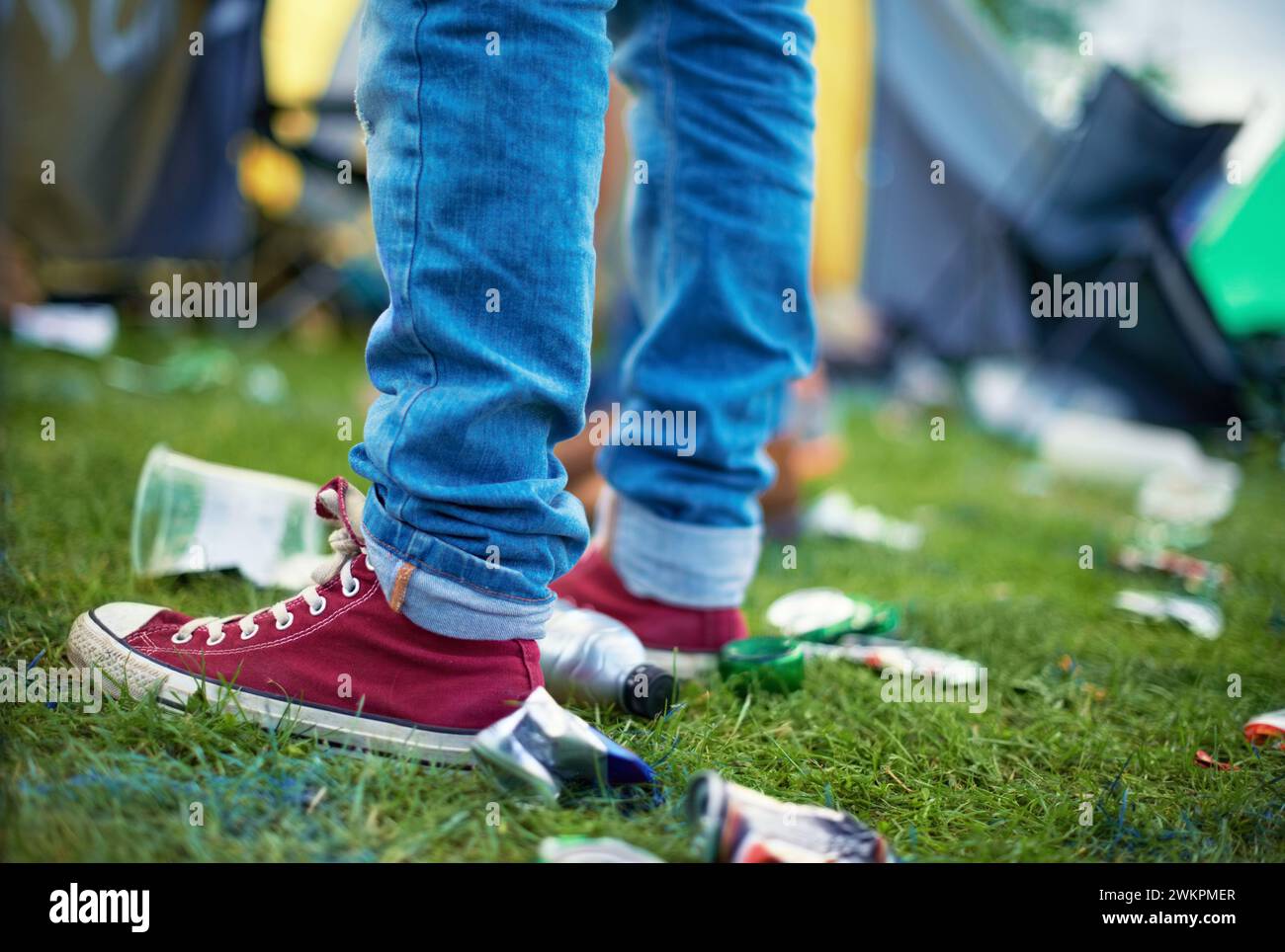 Feet, event and a person with litter on grass and plastic bottles, cans ...