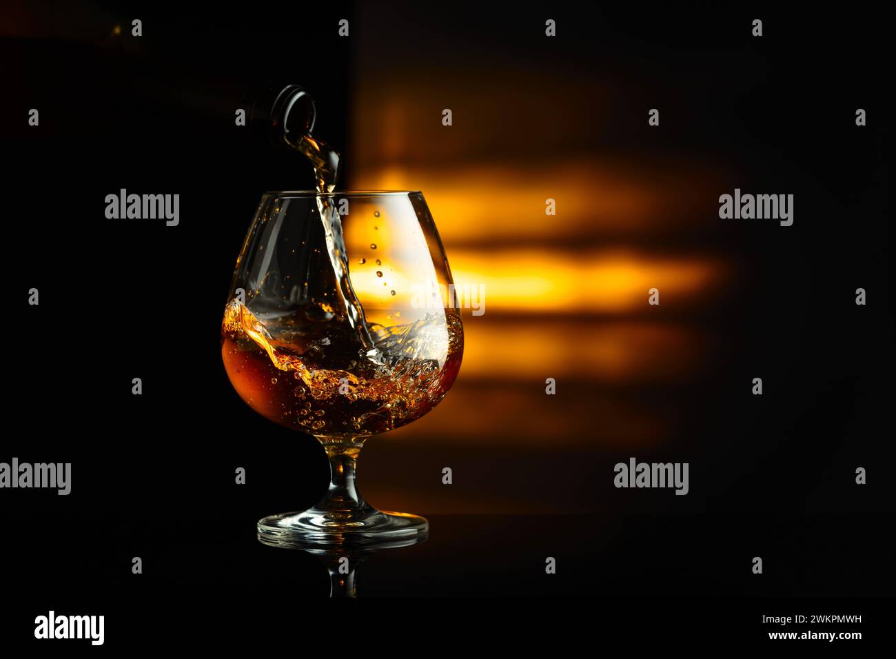 Pouring brandy from a bottle into a snifter on a black reflective ...