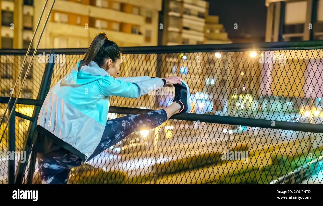 Close up of brunette female runner stretching her legs over bridge ...